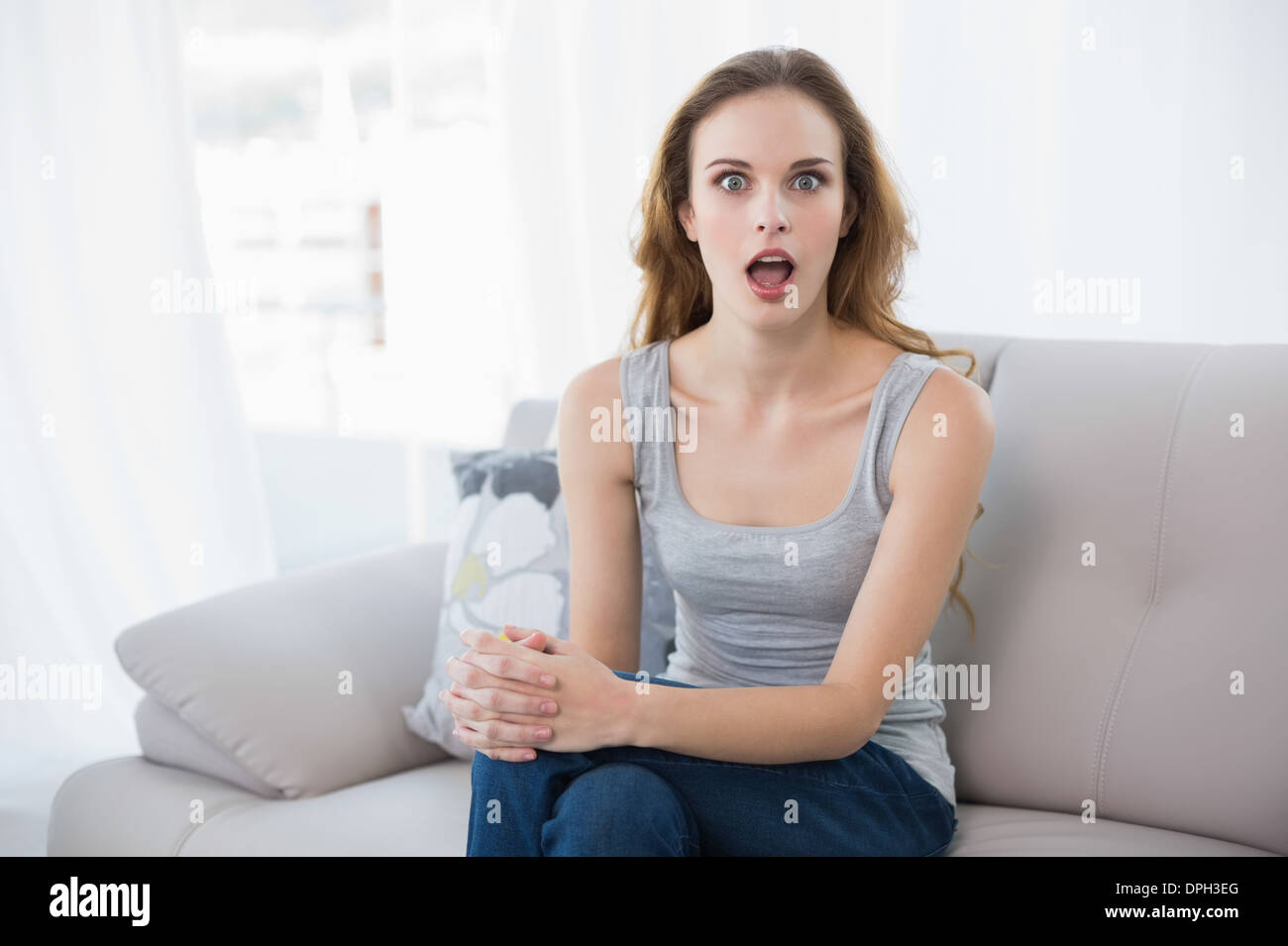 Shocked young woman sitting on couch Stock Photo - Alamy
