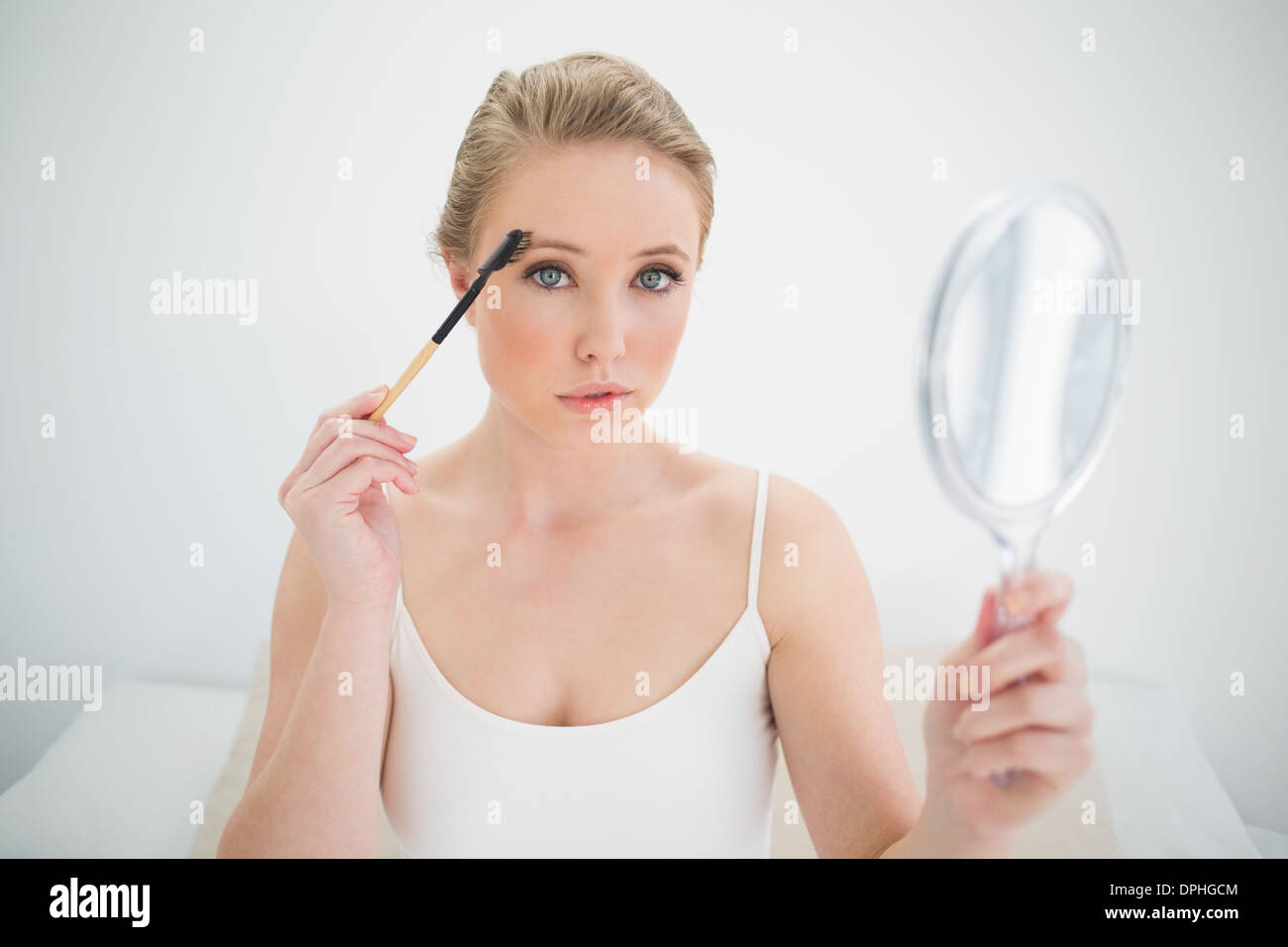 Natural stern blonde holding mirror and using eyebrow brush Stock Photo ...