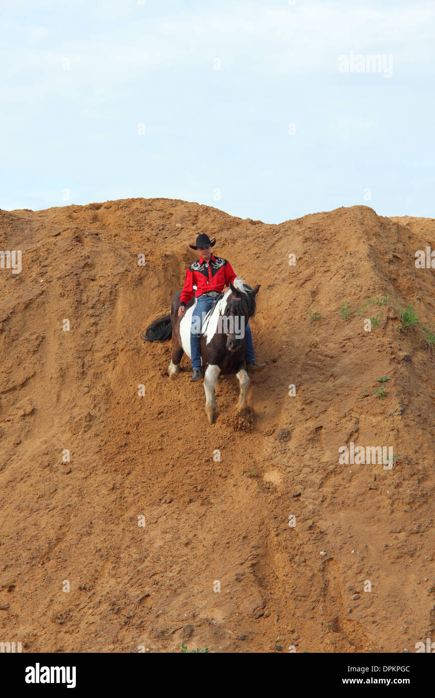 A cowboy riding a quarter horse on top of a rocky, western hilltop ...
