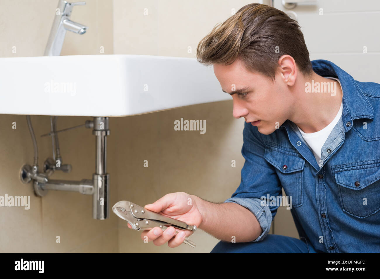 Young plumber with wrench by sink in bathroom Stock Photo - Alamy