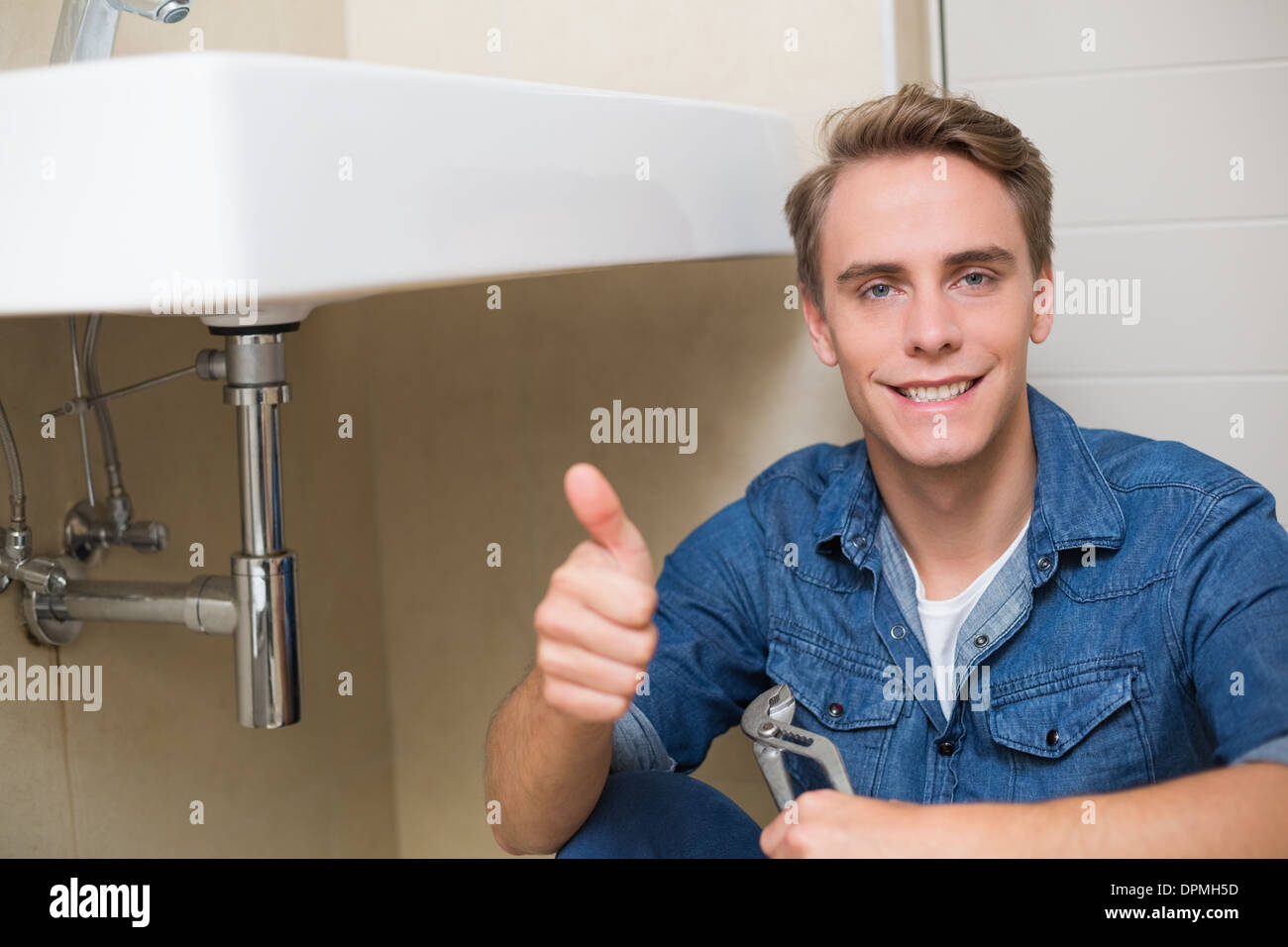 Handsome plumber gesturing thumbs up besides washbasin Stock Photo - Alamy