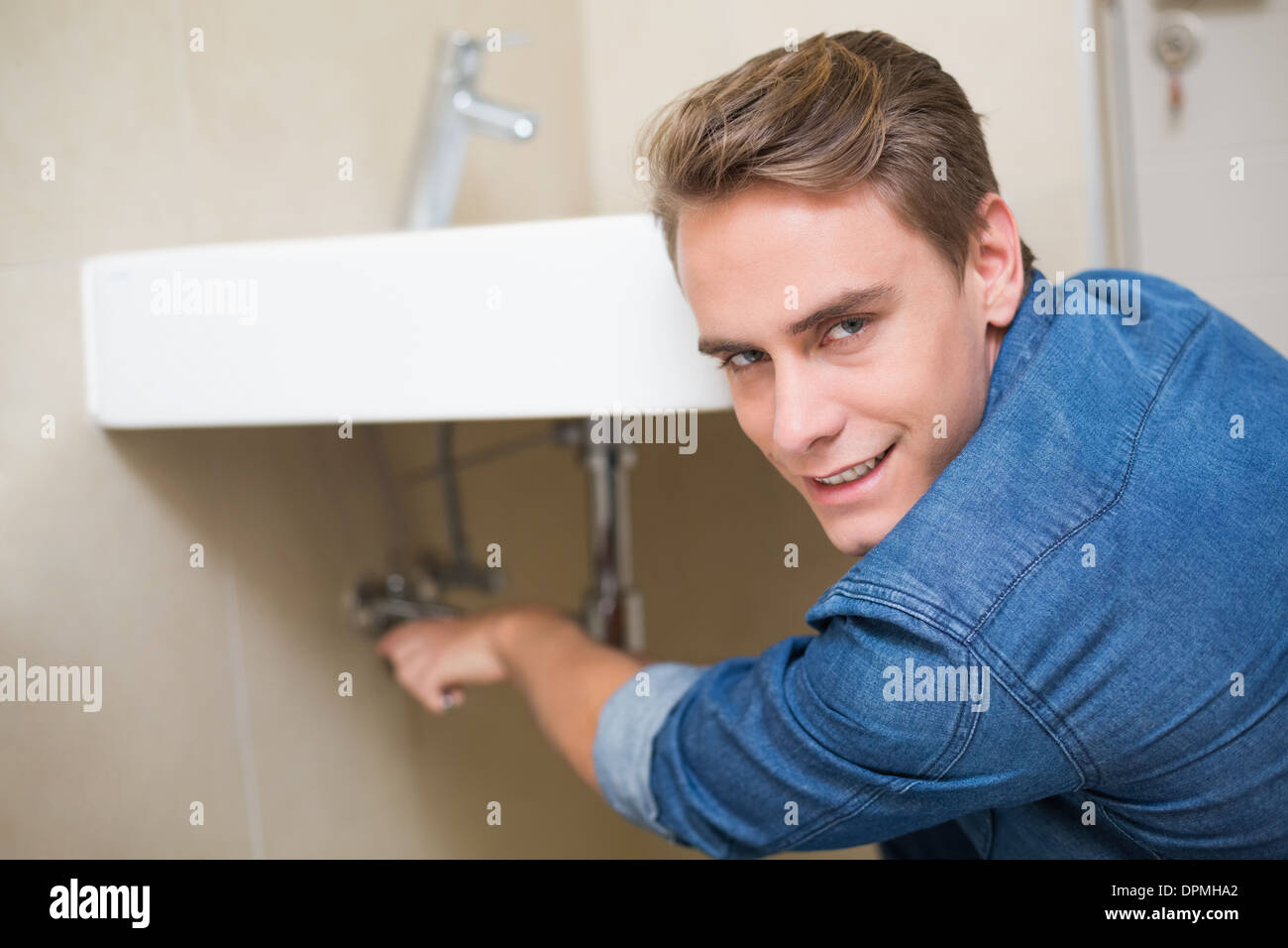 Smiling plumber repairing washbasin drain Stock Photo - Alamy