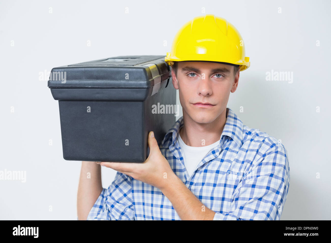 Serious handyman in yellow hard hat carrying toolbox Stock Photo - Alamy