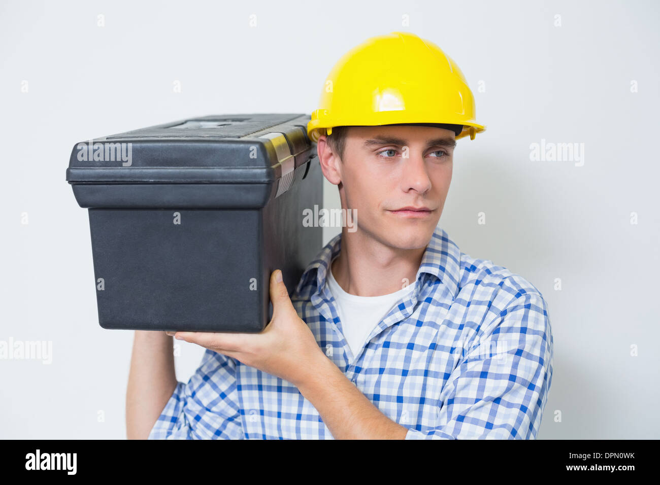 Serious handyman in yellow hard hat carrying toolbox Stock Photo - Alamy