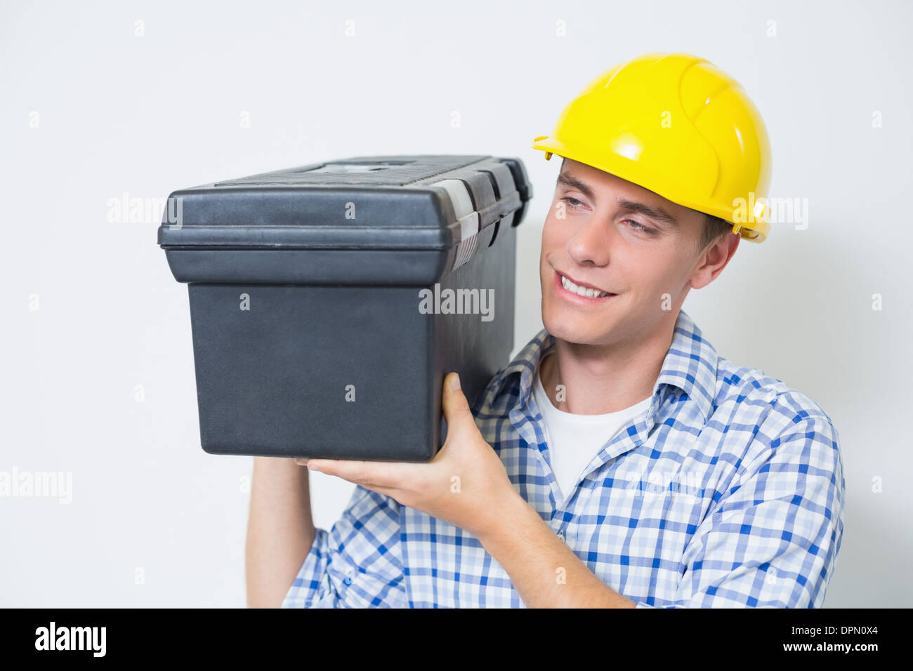 Smiling handyman in yellow hard hat carrying toolbox Stock Photo - Alamy