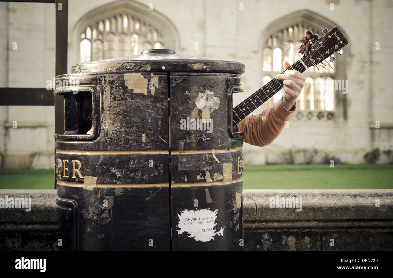 Busker playing a guitar sitting in a waste bin on a street in England ...