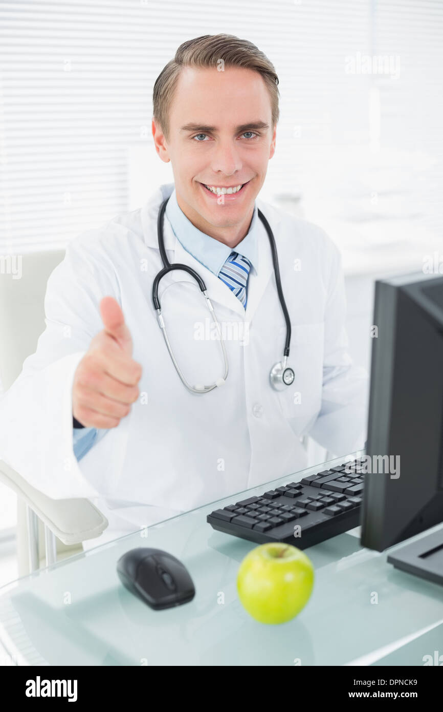 Doctor using computer while gesturing thumbs up at medical office Stock ...