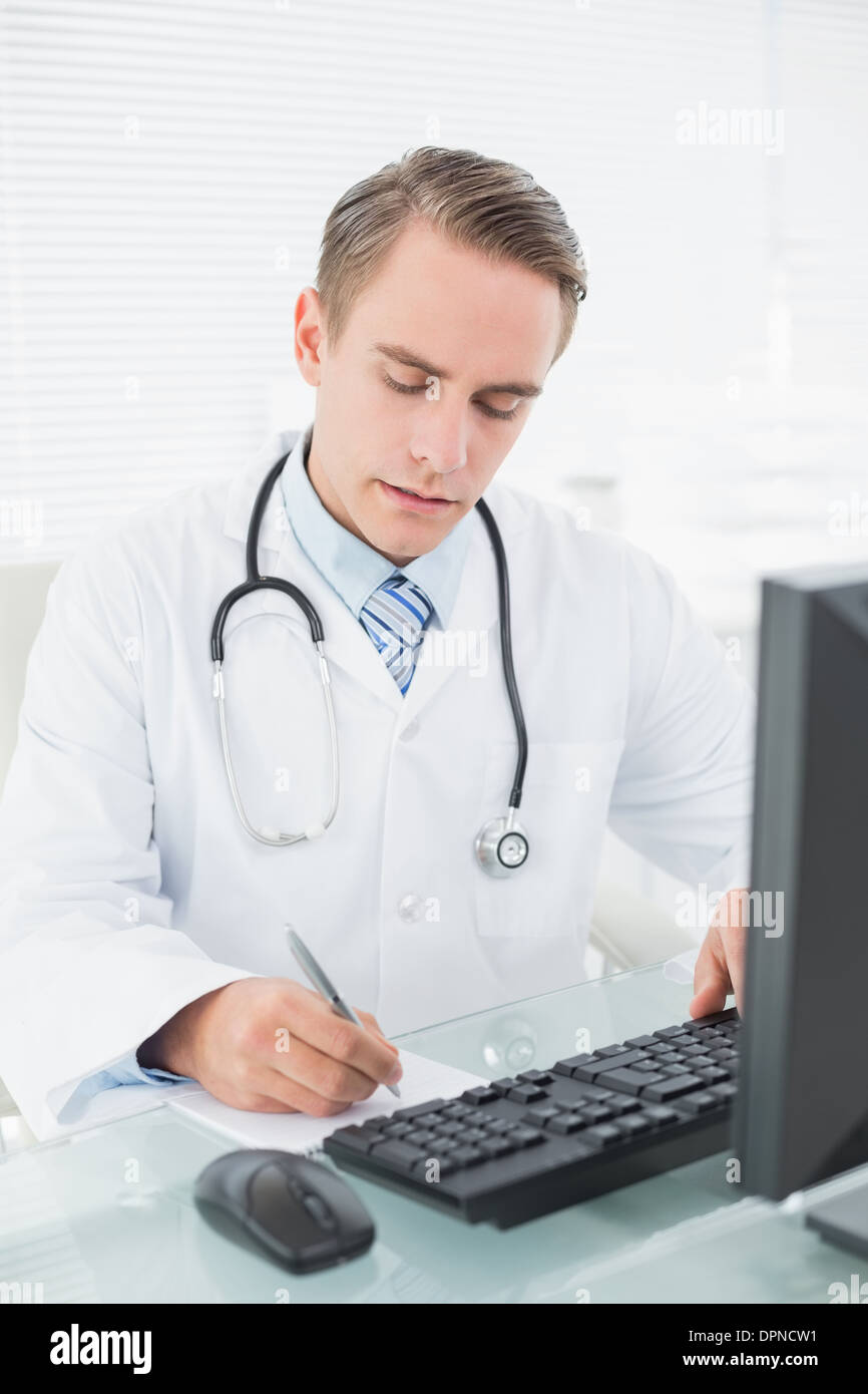 Doctor writing a note while using computer at medical office Stock ...
