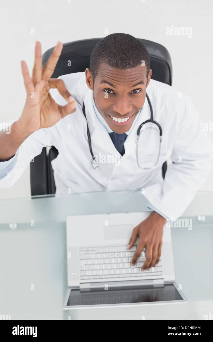Overhead of a smiling male doctor with laptop gesturing okay sign Stock ...