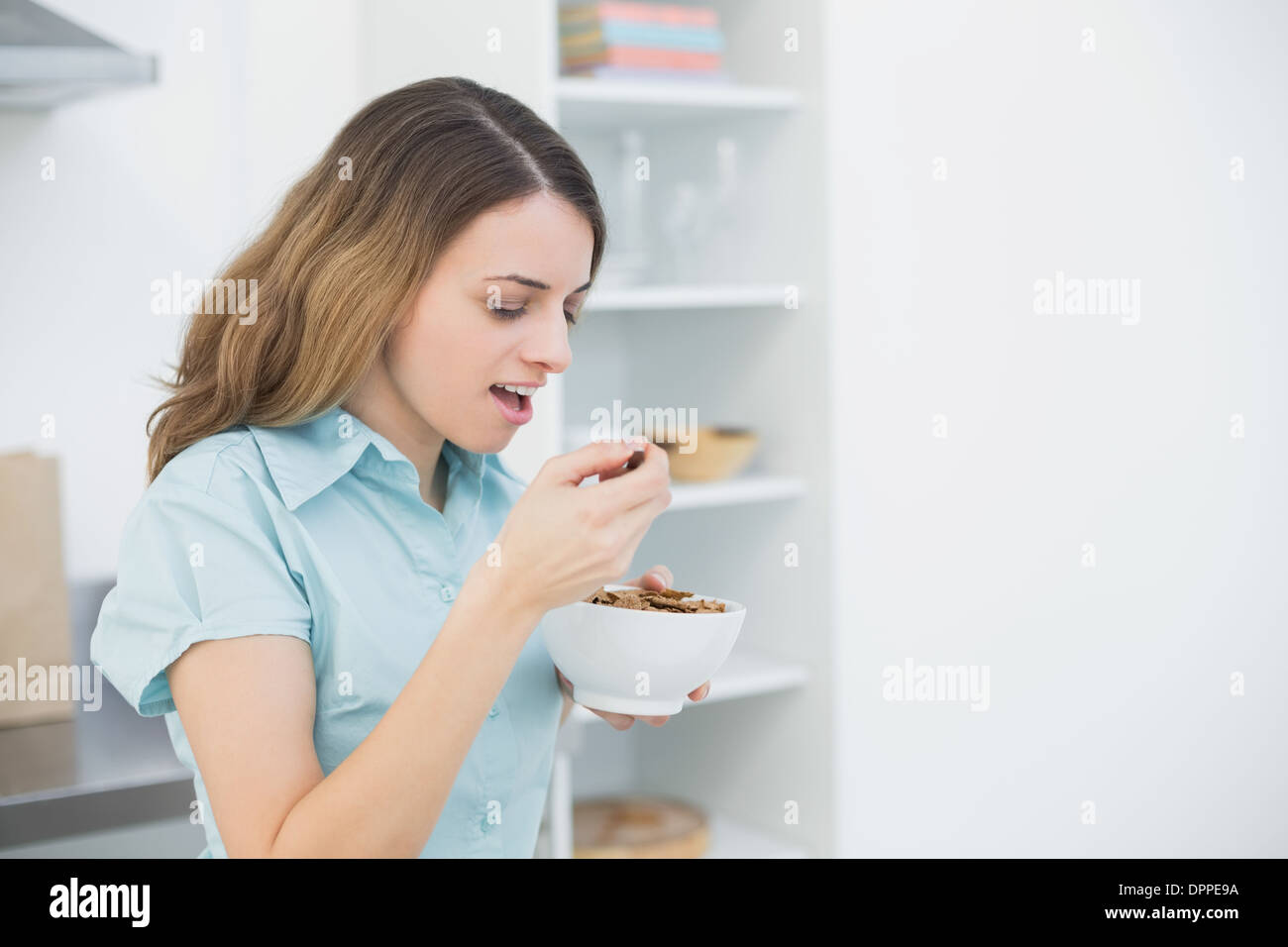 Lovely woman eating cereals while standing in her kitchen Stock Photo ...