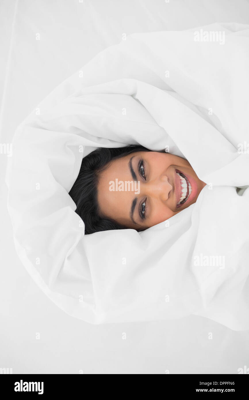 Cheerful woman lying under cover on her bed Stock Photo - Alamy