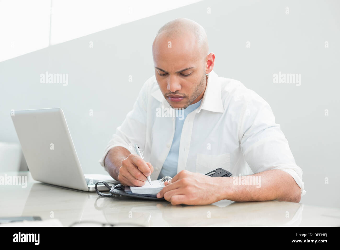 Casual serious man with laptop writing in diary Stock Photo - Alamy