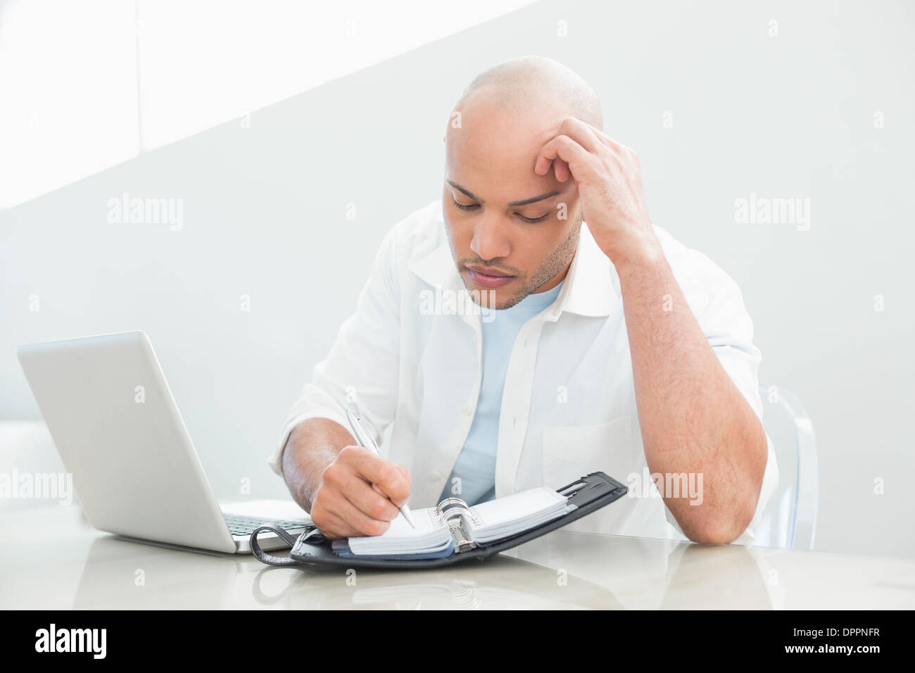 Casual serious man with laptop writing in diary Stock Photo - Alamy