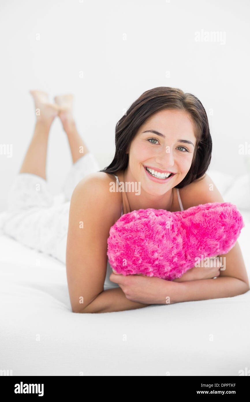 Smiling woman lying with heart shaped pillow in bed Stock Photo - Alamy