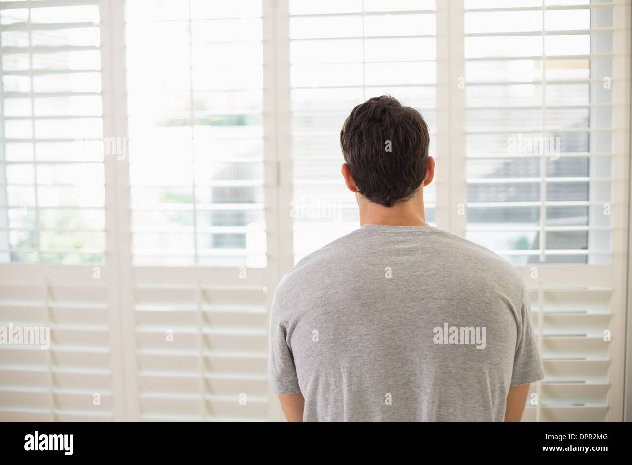 Rear view of man looking through window blinds at bright room Stock ...