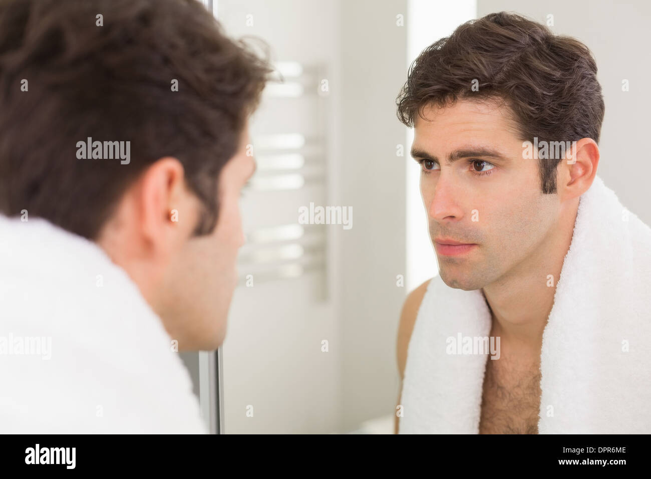 Serious young man looking at self in bathroom mirror Stock Photo - Alamy
