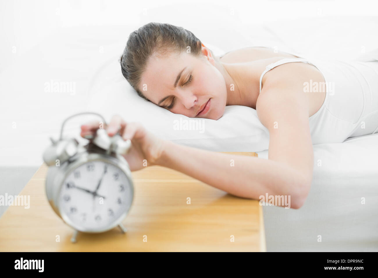 Sleepy woman in bed extending hand to alarm clock Stock Photo - Alamy