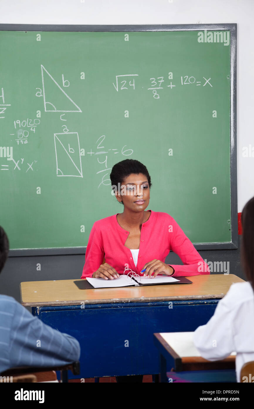 Teacher Sitting At Desk With Students In Foreground Stock Photo - Alamy