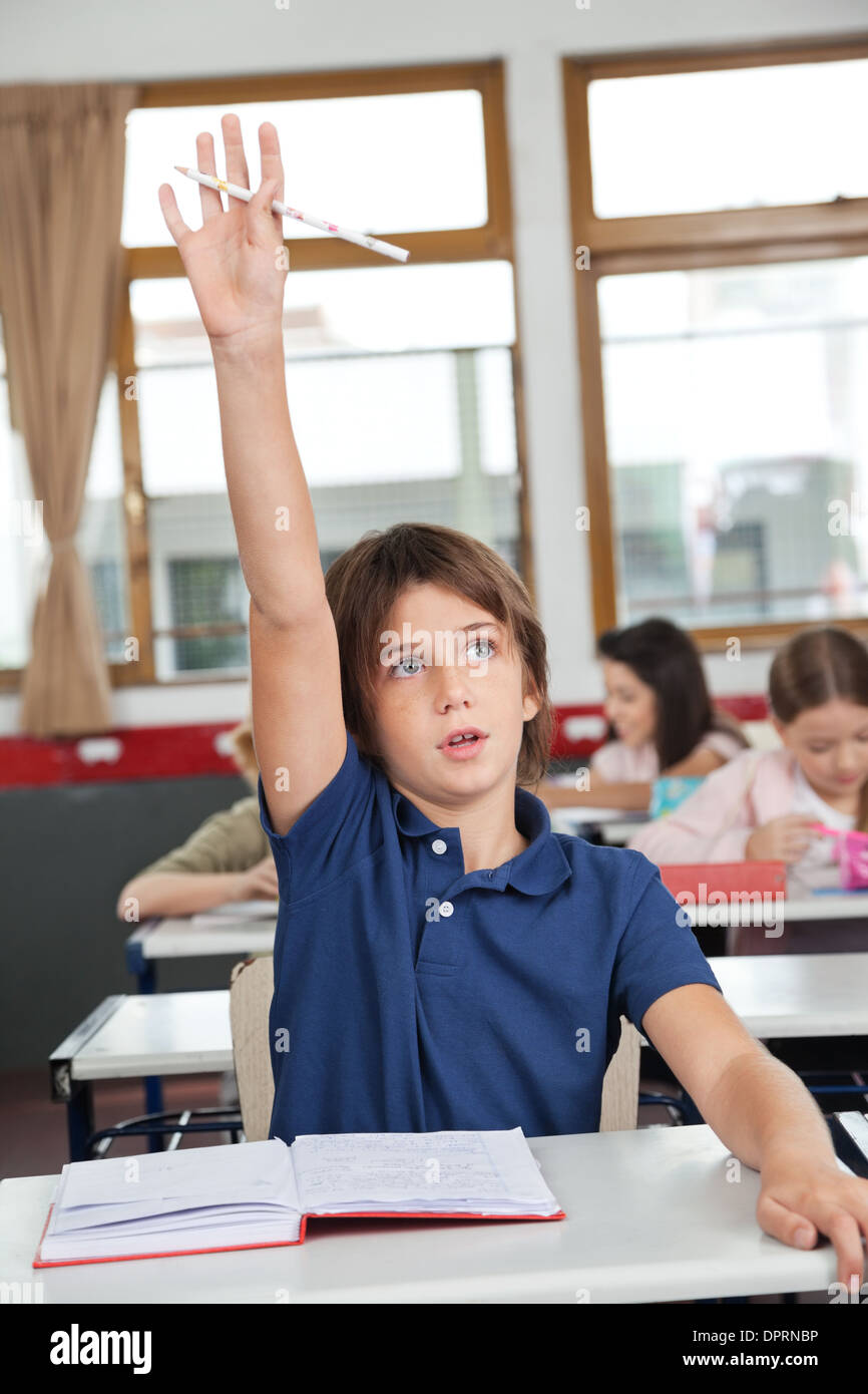 Cute Schoolboy Raising Hand In Classroom Stock Photo - Alamy