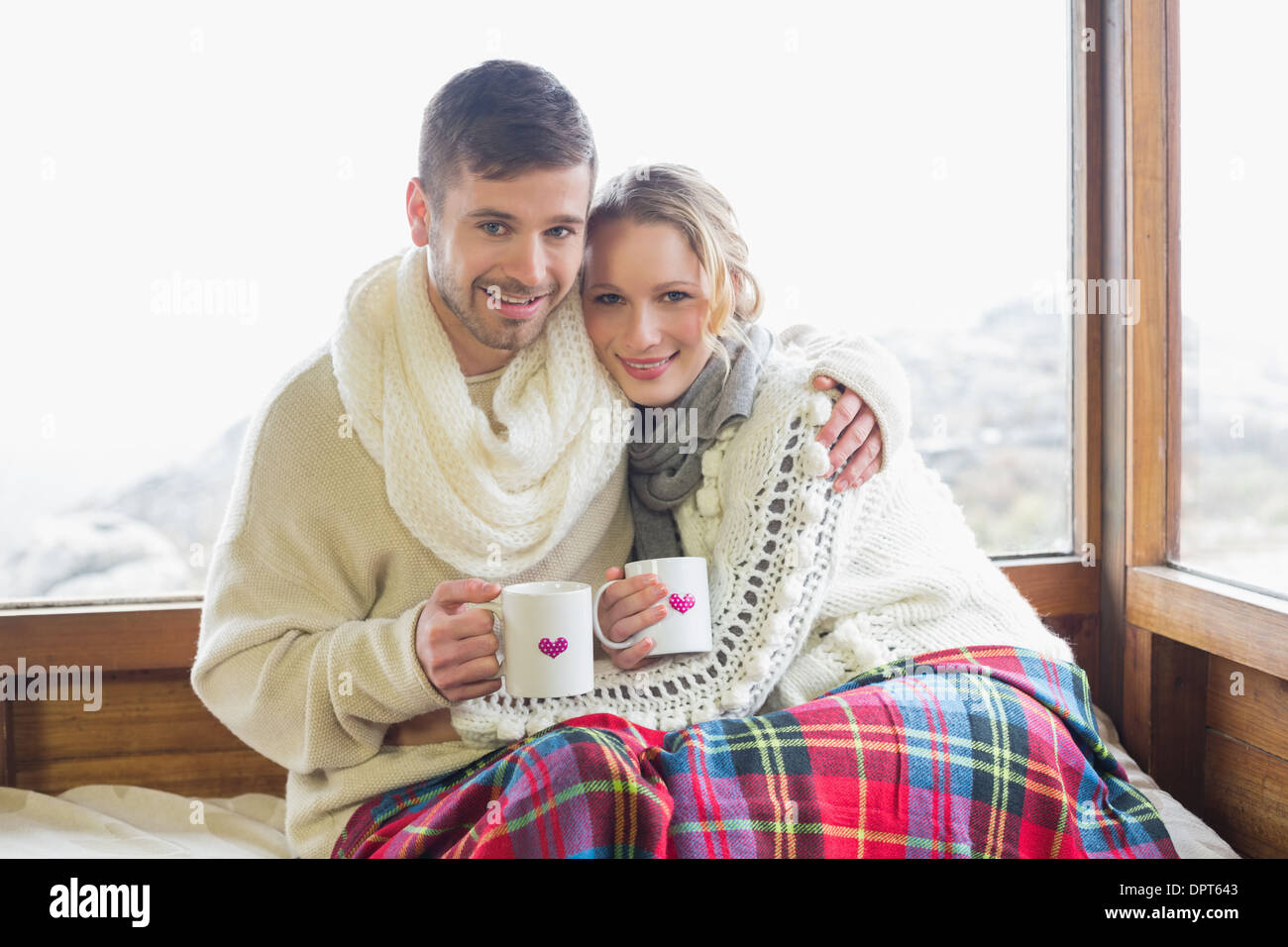 Loving couple in winter wear with cups against window Stock Photo - Alamy