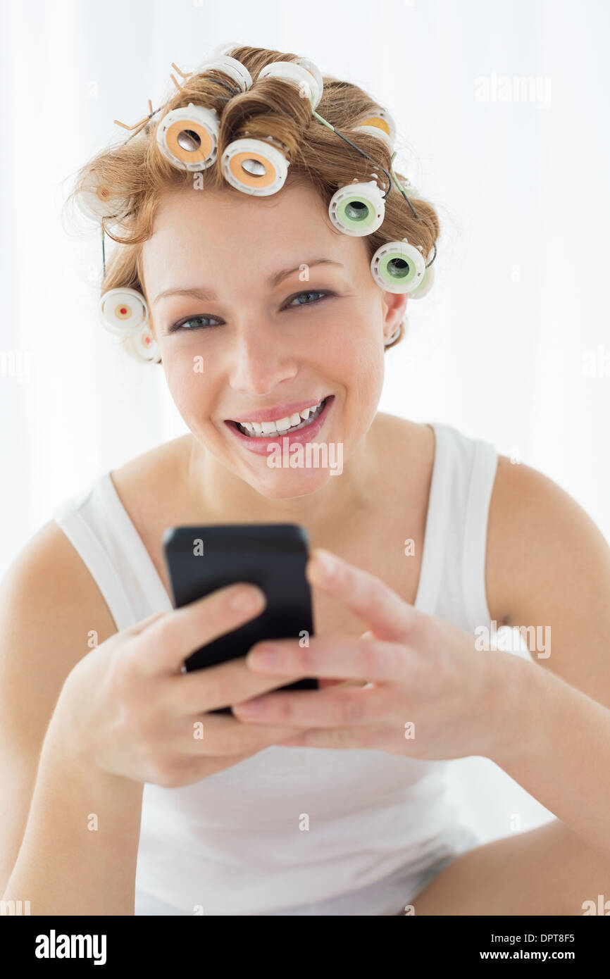 Woman in hair curlers text messaging on bed Stock Photo - Alamy