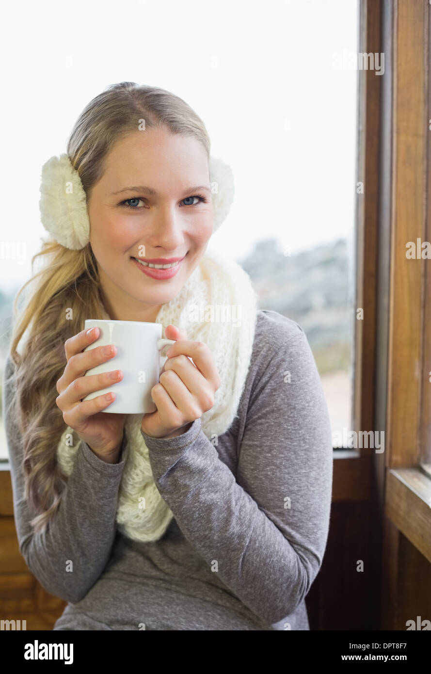 Smiling woman wearing earmuff with cup against window Stock Photo - Alamy