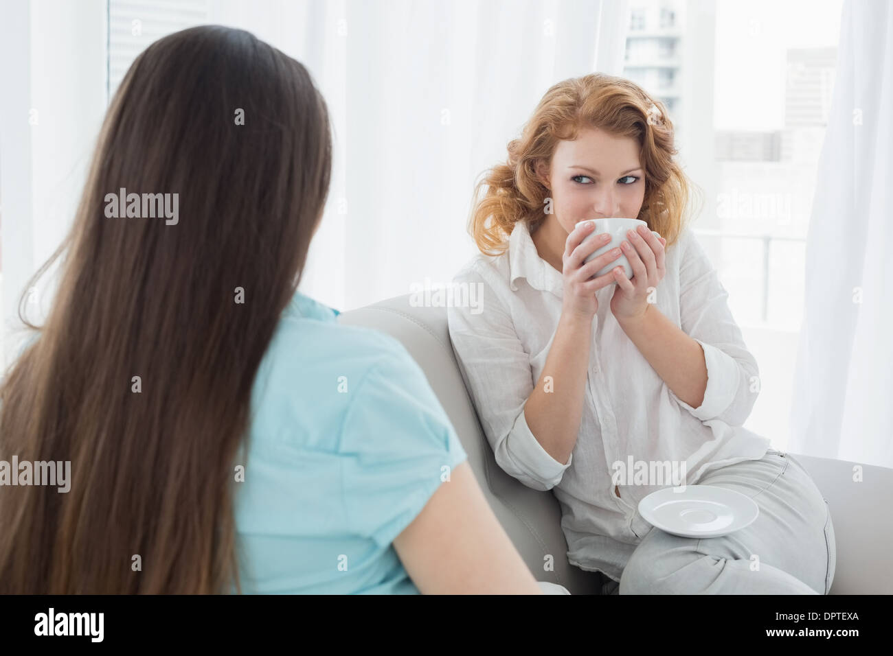 Female friends sitting on sofa in the living room Stock Photo - Alamy