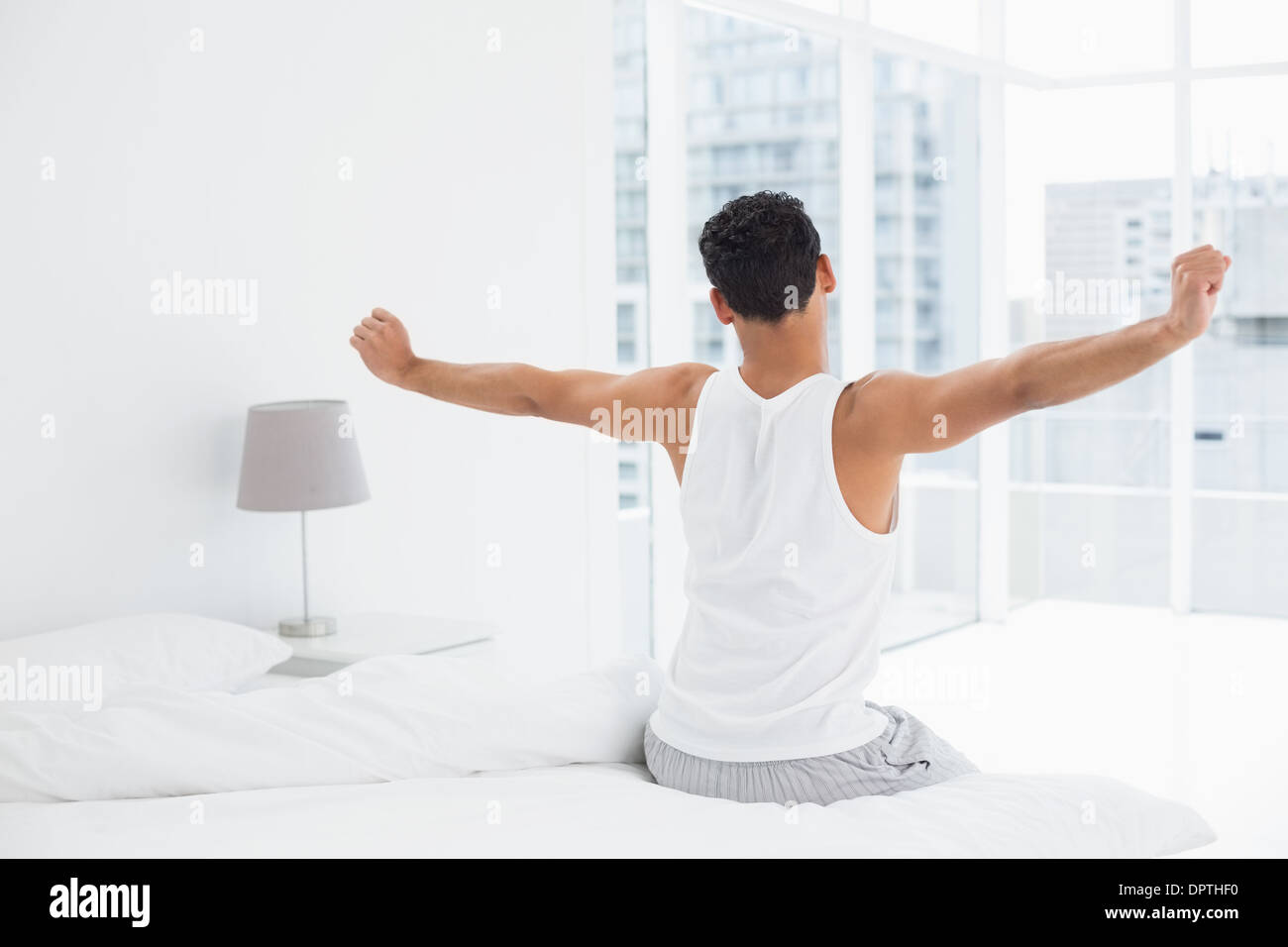 Rear view of a young man stretching arms in bed Stock Photo - Alamy