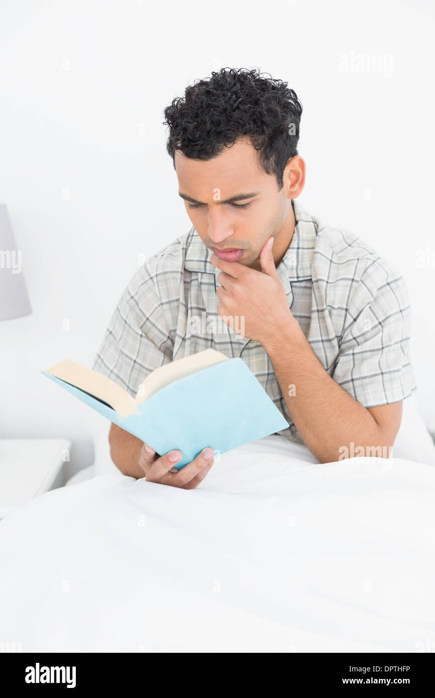 Serious young man reading book in bed Stock Photo - Alamy