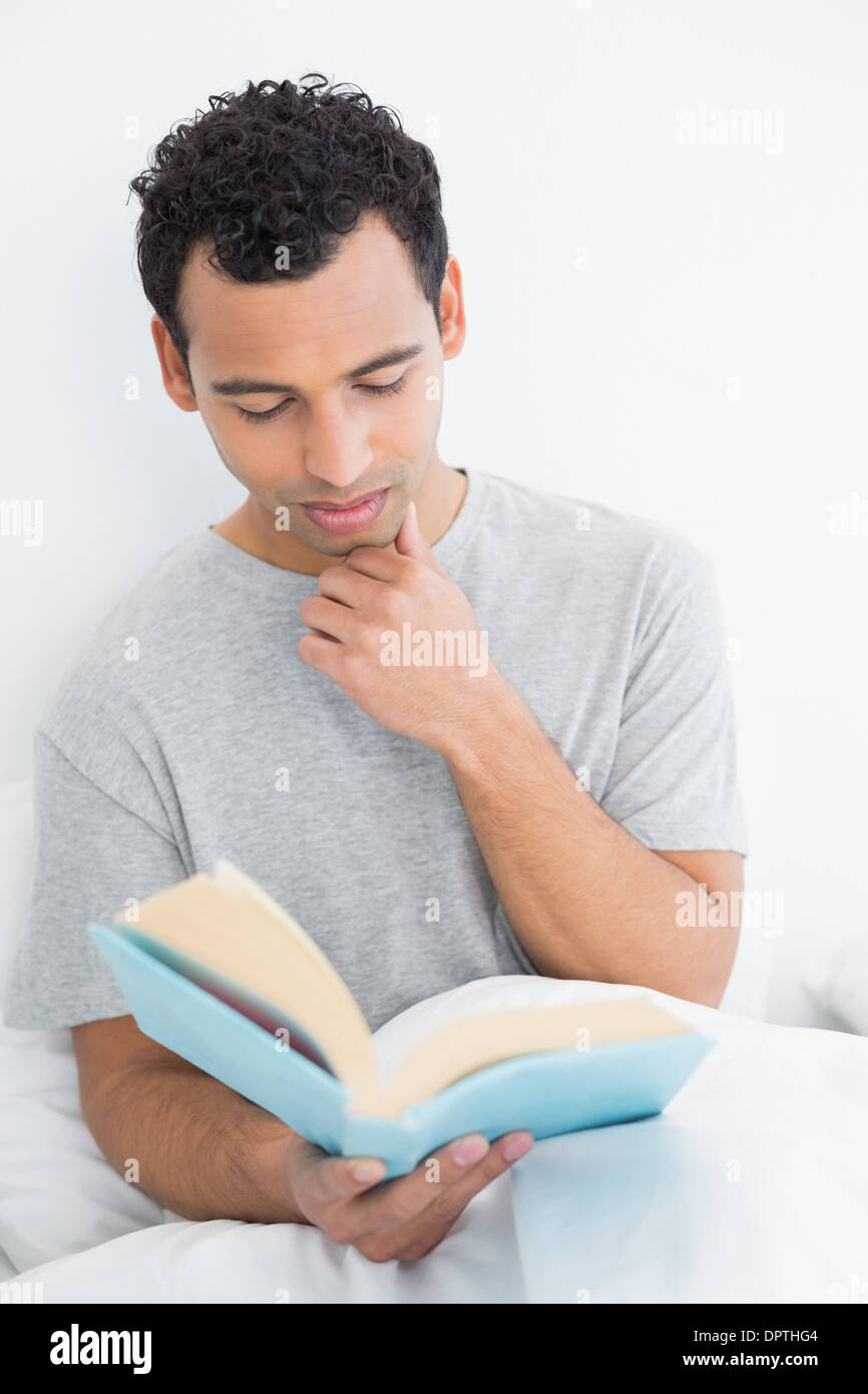 Serious relaxed man reading book in bed Stock Photo - Alamy