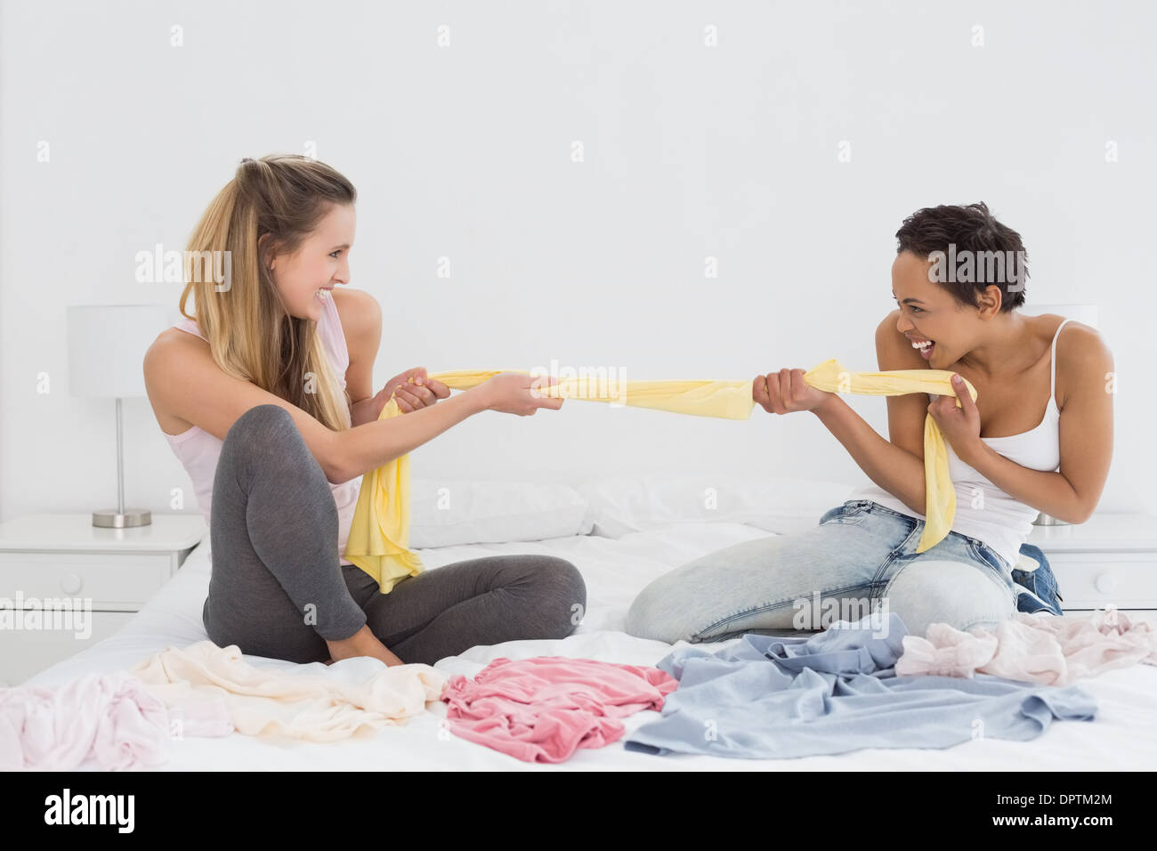Female friends jokingly fighting over clothes on bed Stock Photo - Alamy