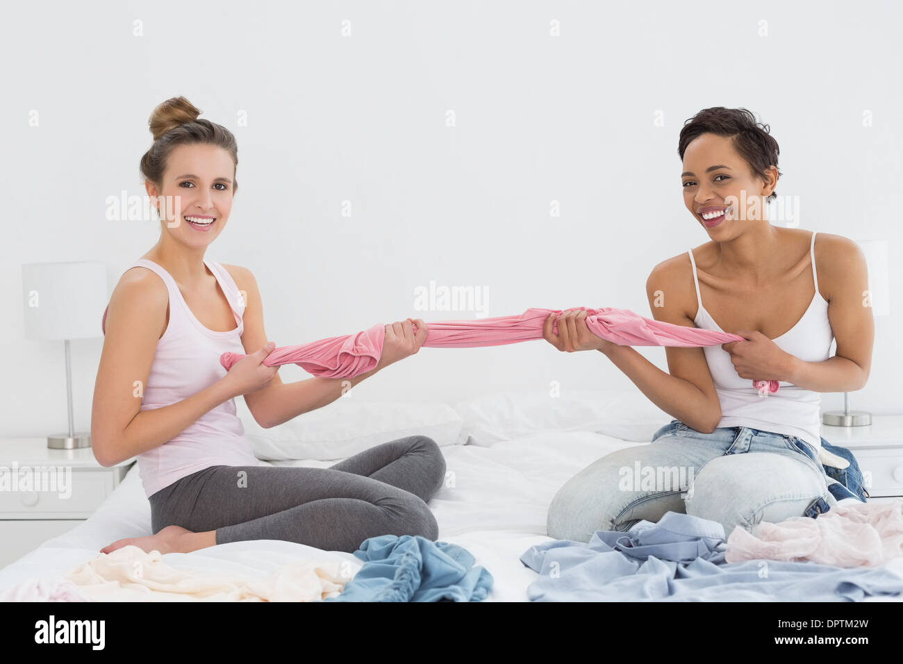 Pretty friends jokingly fighting over clothes on bed Stock Photo - Alamy