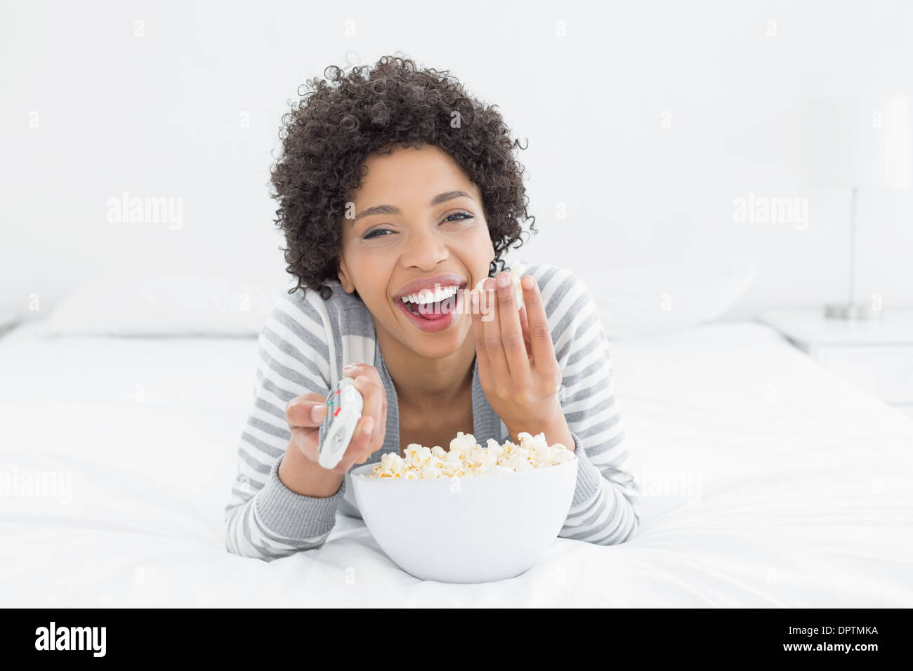 Cheerful woman with remote control and popcorn bowl in bed Stock Photo ...