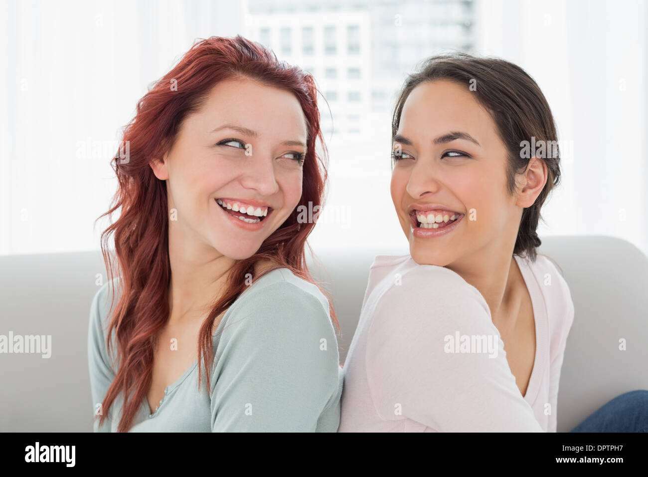 Beautiful young female friends sitting back to back at home Stock Photo ...
