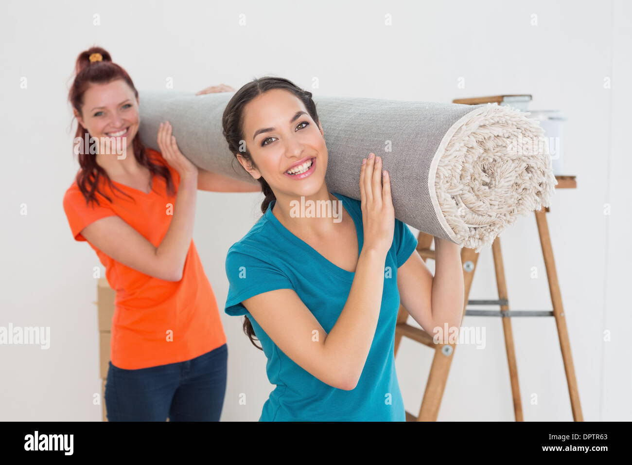 Female friends carrying rolled rug after moving in a house Stock Photo ...