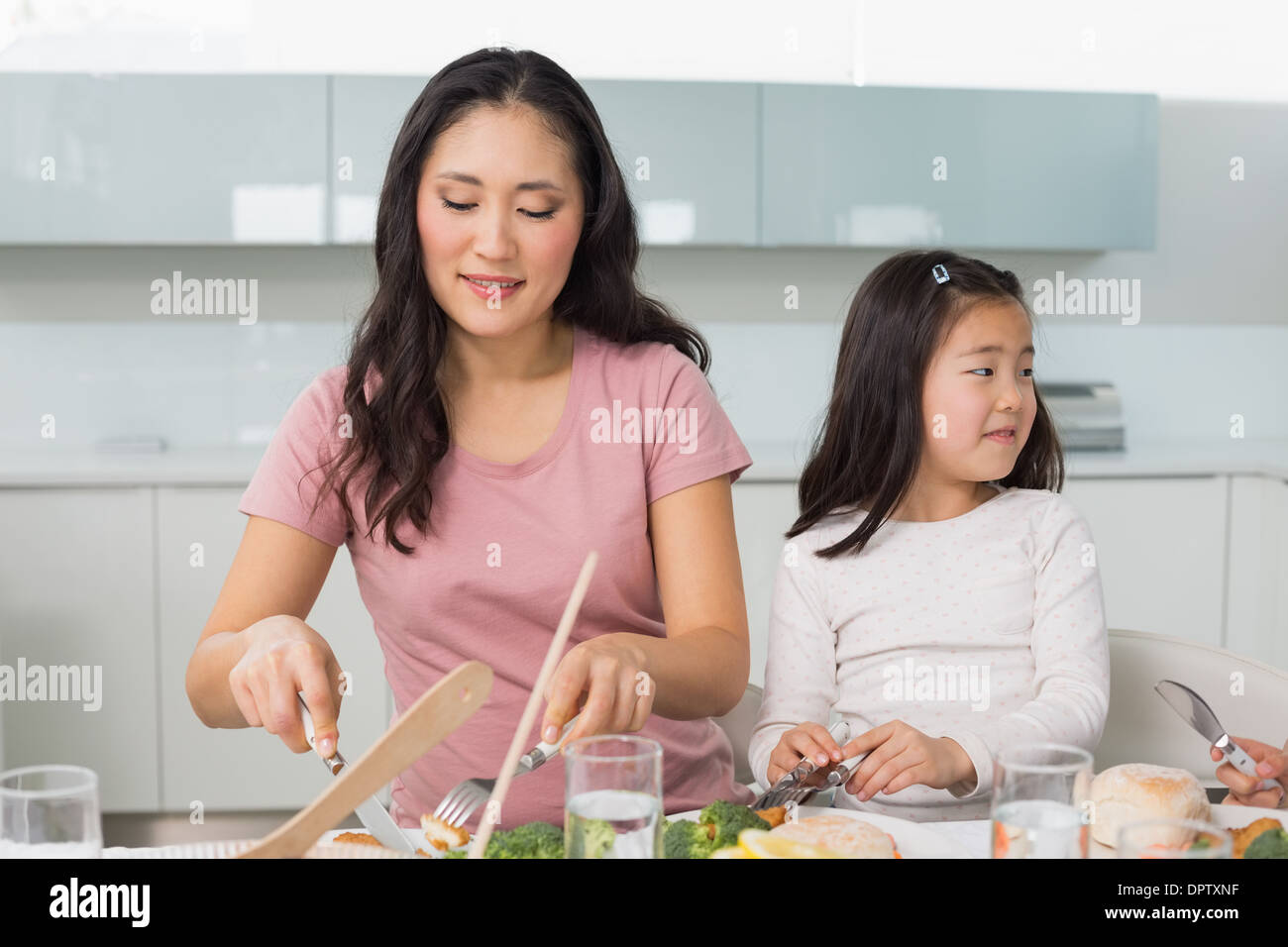 Little girl and mother eat food in kitchen Stock Photo - Alamy