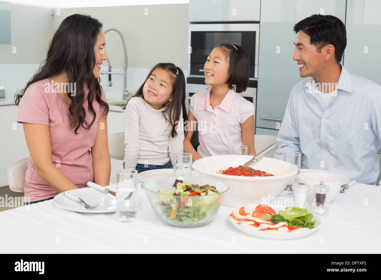 Smiling family of four sitting at dining table in kitchen Stock Photo ...