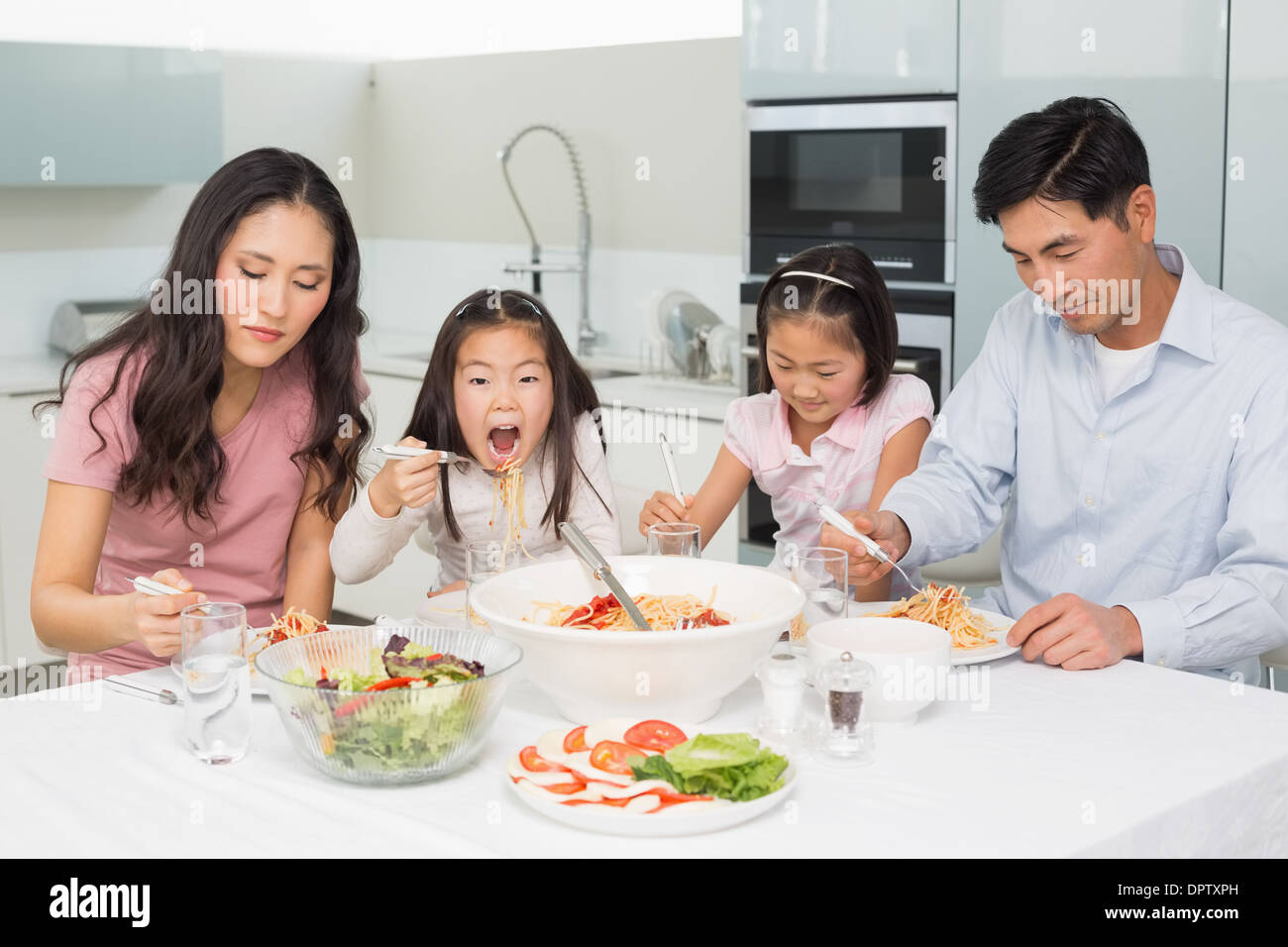 Happy family of four enjoying spaghetti lunch in kitchen Stock Photo ...