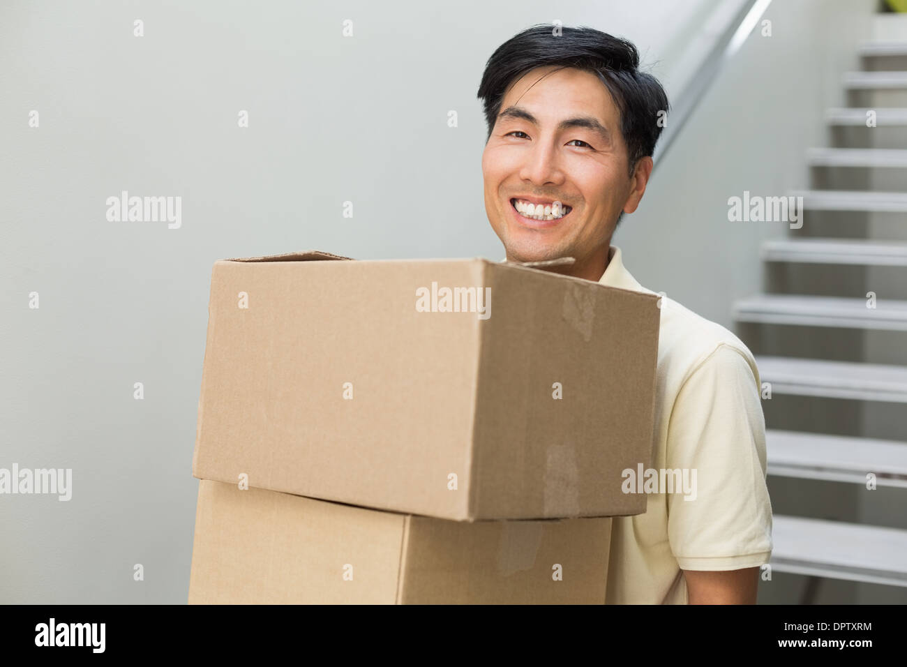 Smiling young man carrying boxes against staircase Stock Photo - Alamy