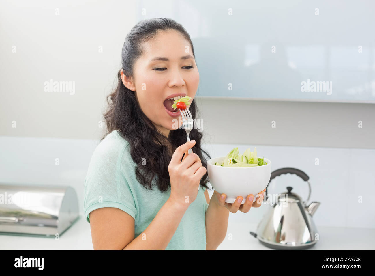 Side view of a young woman eating salad in kitchen Stock Photo - Alamy