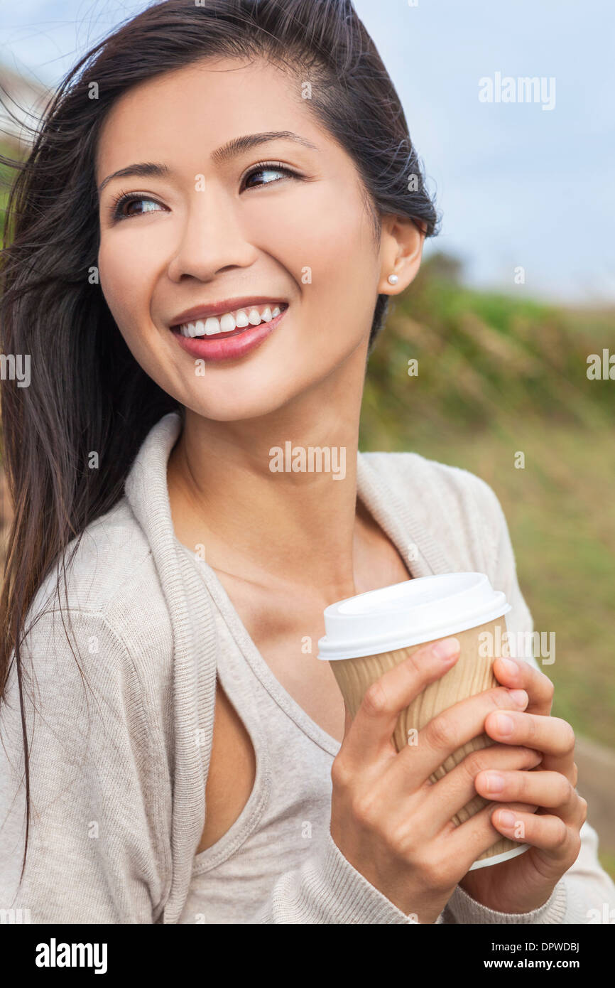 Beautiful young Asian Chinese woman or girl outside, smiling and drinking a takeaway cup of ...
