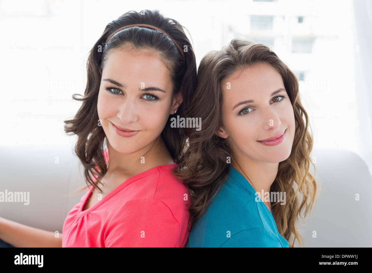 Smiling friends sitting back to back in living room Stock Photo - Alamy