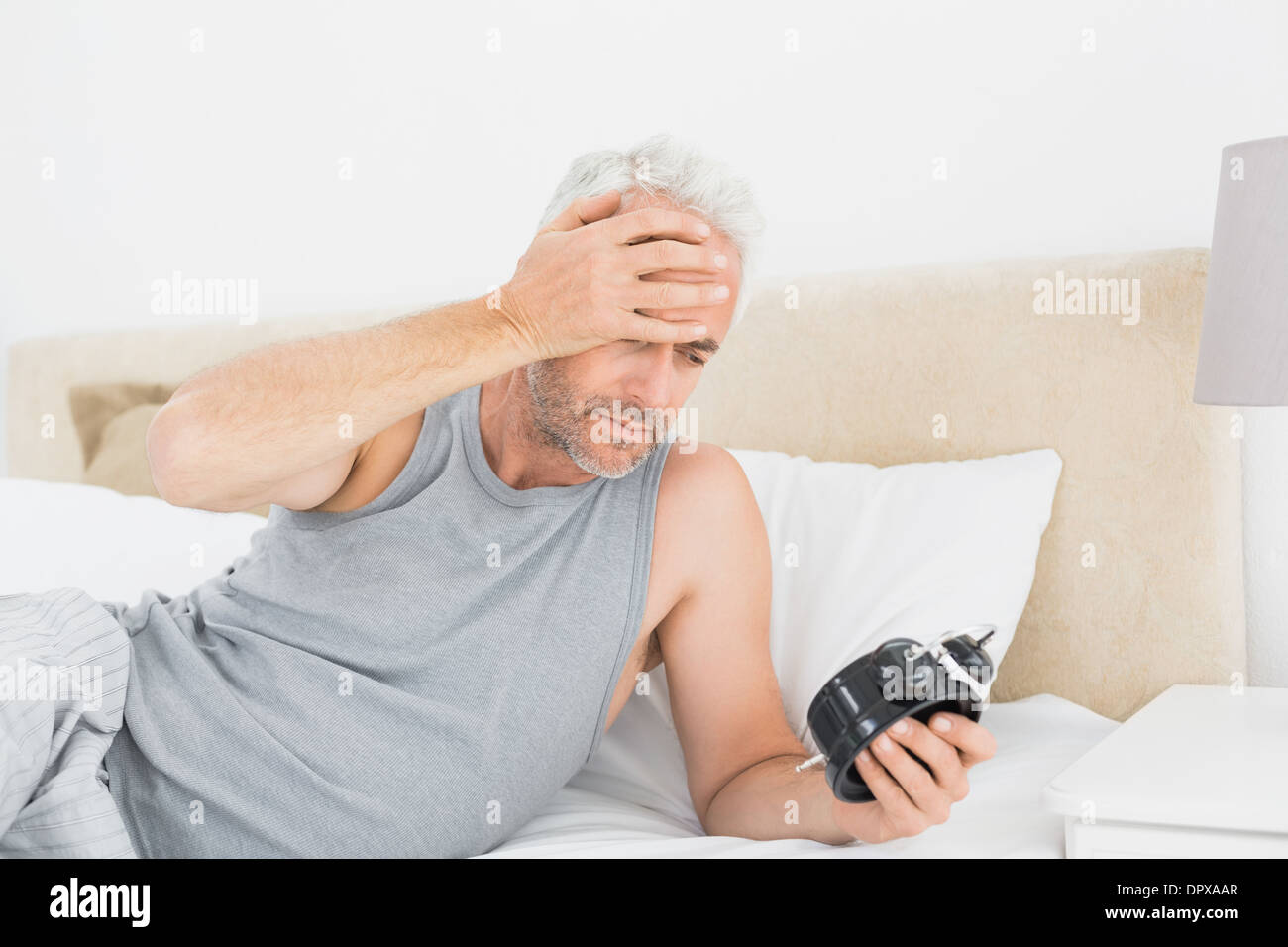 Man looking at alarm clock in bed Stock Photo - Alamy