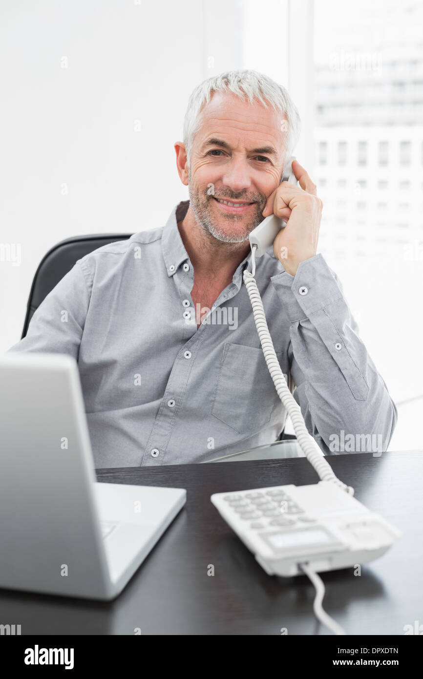 Businessman using telephone in front of laptop at office desk Stock ...