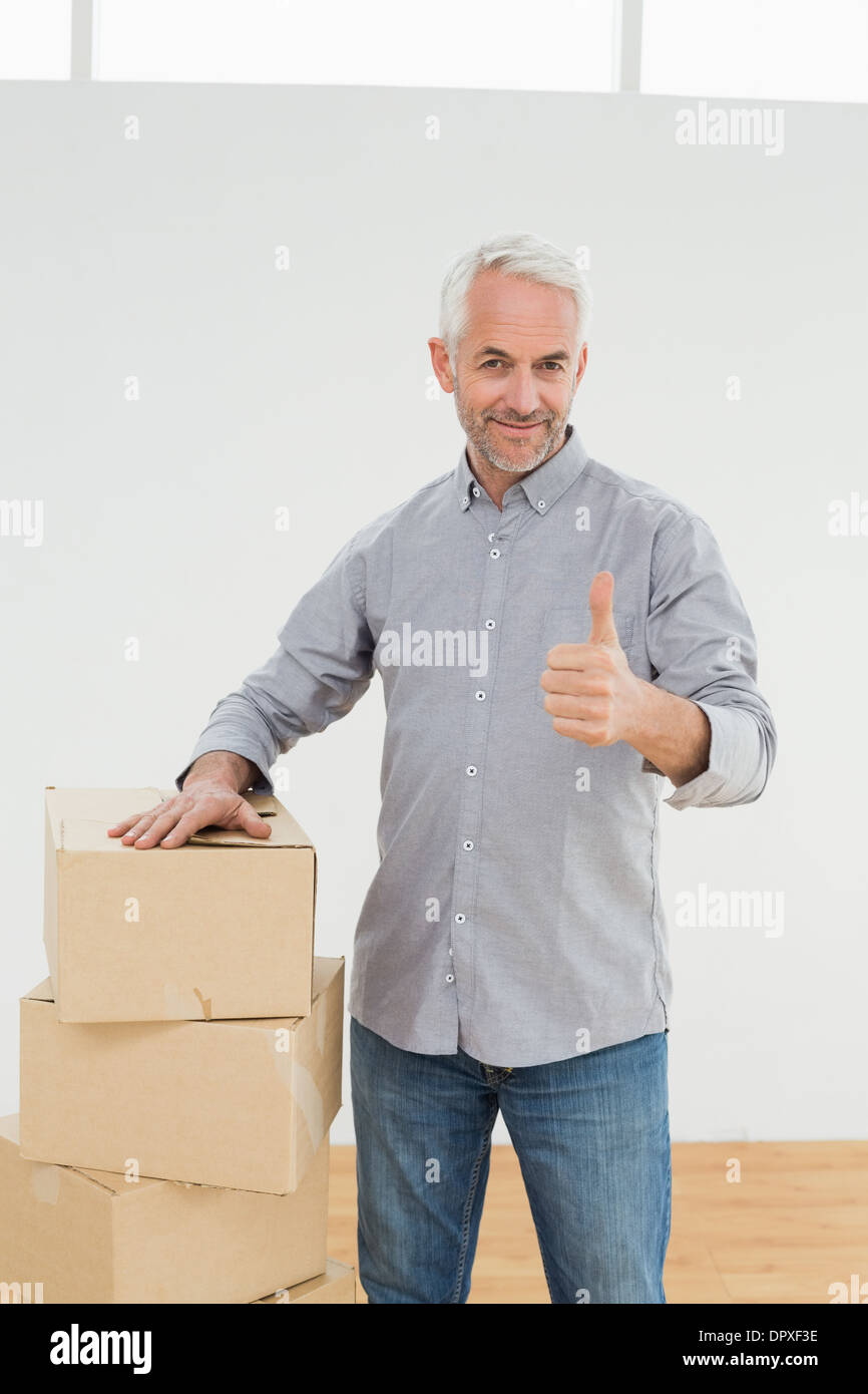 Smiling man with boxes gesturing thumbs up in a new house Stock Photo ...