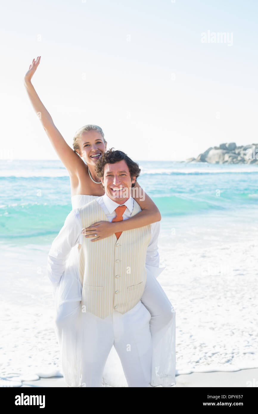 Waving bride getting a piggy back from husband smiling at camera Stock ...