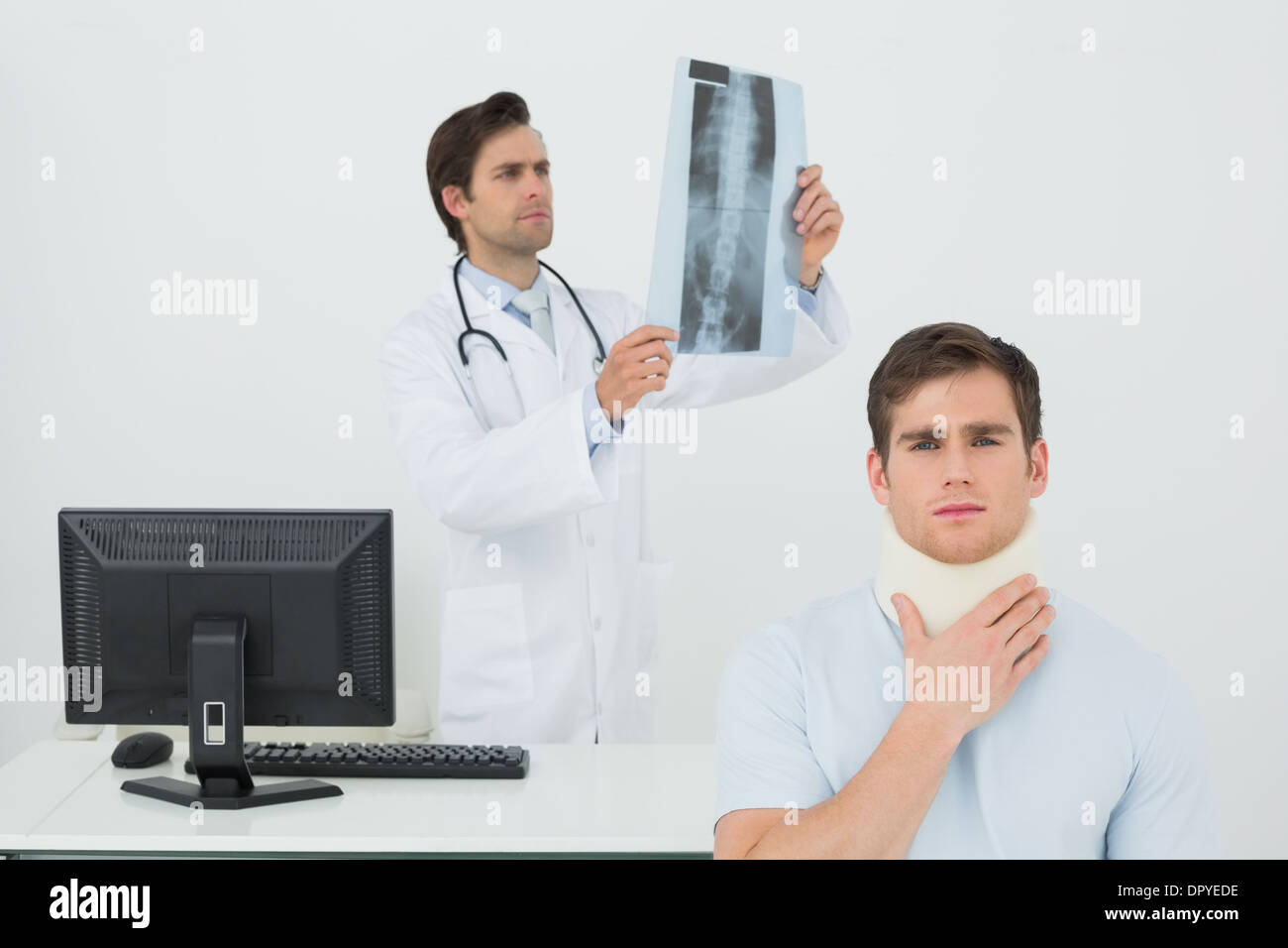 Patient in surgical collar while doctor examining spine x-ray behind ...