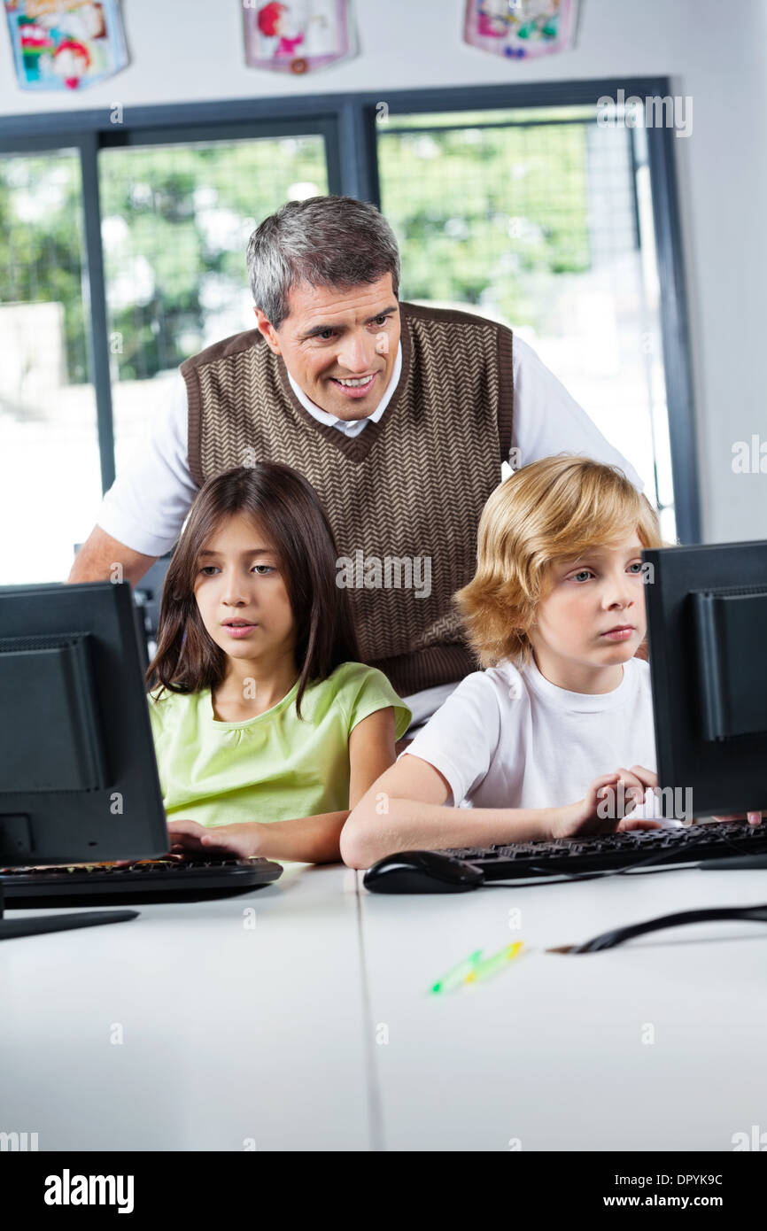 Teacher Looking At Schoolchildren Using Desktop Pc Stock Photo - Alamy