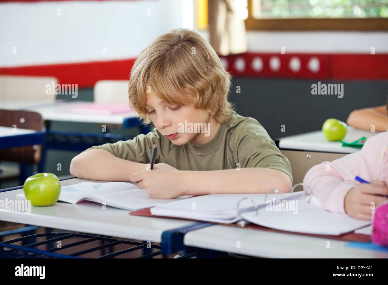 Schoolboy Writing On Book In Classroom Stock Photo - Alamy