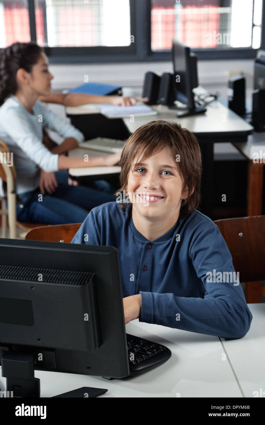 Happy Schoolboy Sitting With Computer At Desk Stock Photo - Alamy